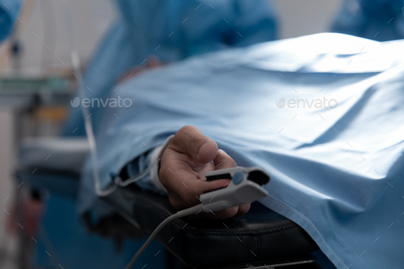 Patient lying on surgical bed wearing fingertip pulse oximeter in ...