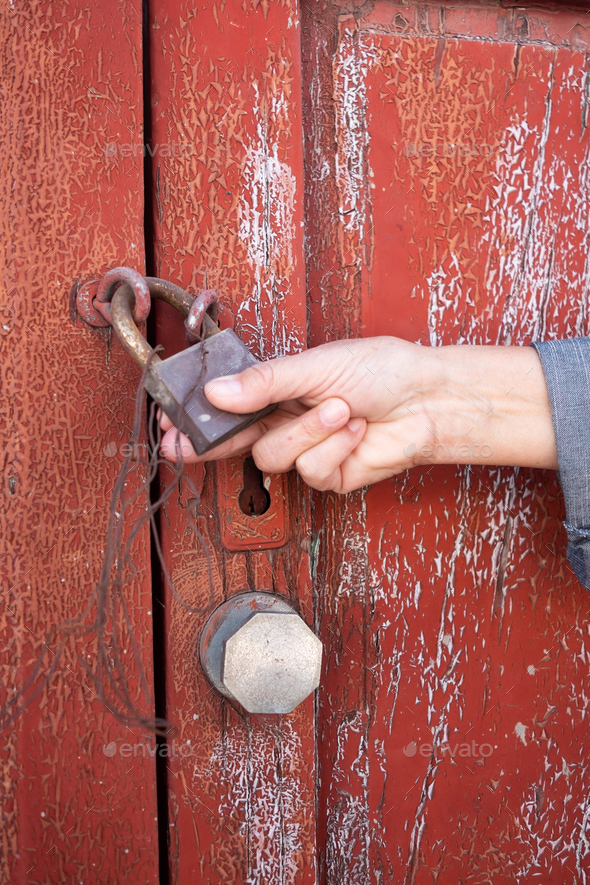 Caucasian woman hand tries to unlock an old padlocked door. Red and ...