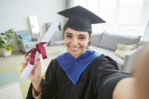 Smiling female graduate taking selfie Stock Photo by seventyfourimages