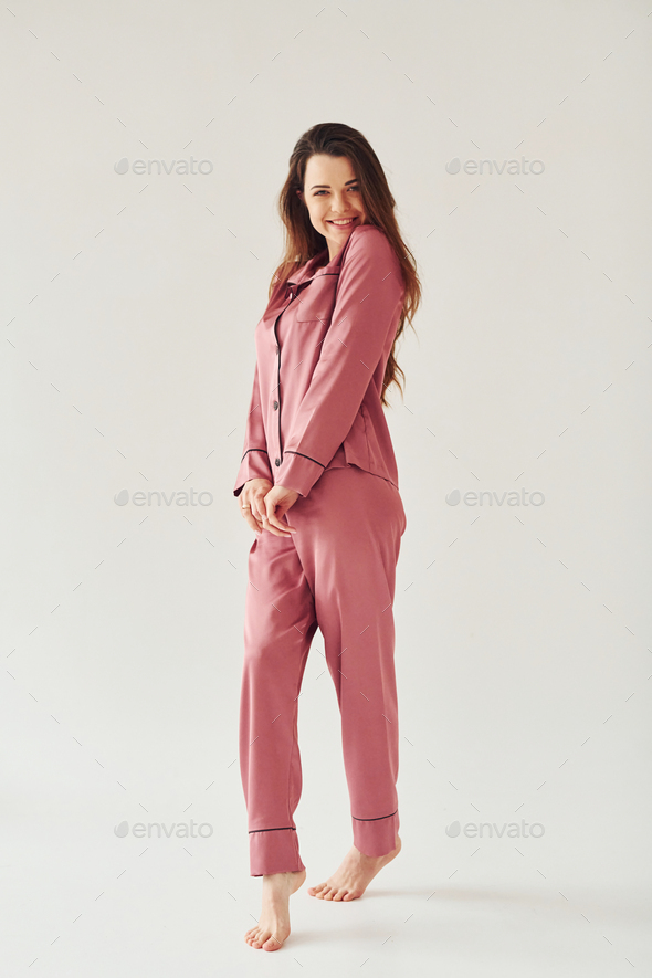 Cheerful young woman in pajamas standing indoors against white ...