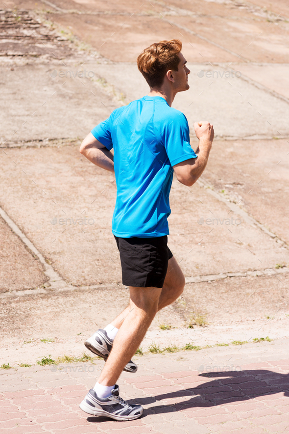 Enjoying a morning run. Side view of young man running along the road ...