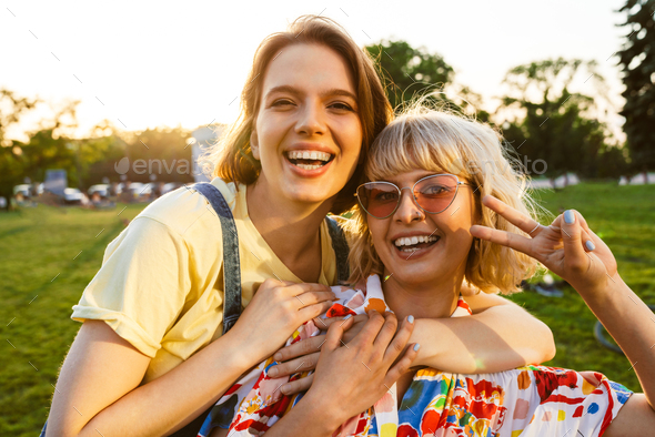 Image of two women gesturing peace sign and hugging while walking Stock ...
