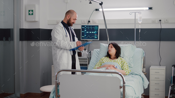 Assistant with dark skin helping patient to sit comfortable in hospital ...