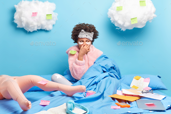 Displeased ethnic woman smells something stinky in bed holds breath ...