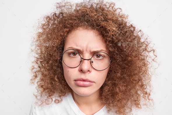 Headshot of angry annoyed young European woman with curly bushy hair ...