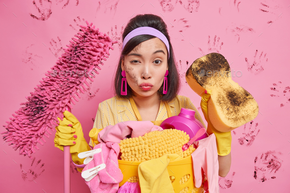 Scrupulous young Asian woman keeps lips folded looks attentively at ...