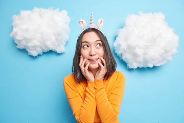 Portrait of pleased young Asian woman looks with dreamy expression ...