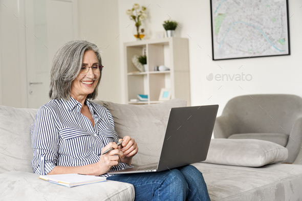 Happy mature mid age woman working on laptop computer from home office ...