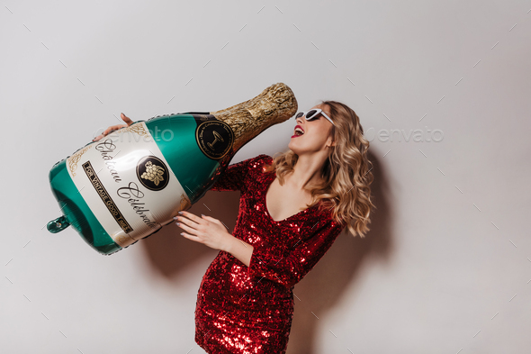 Laughing girl with toy bottle of wine dancing on white background ...