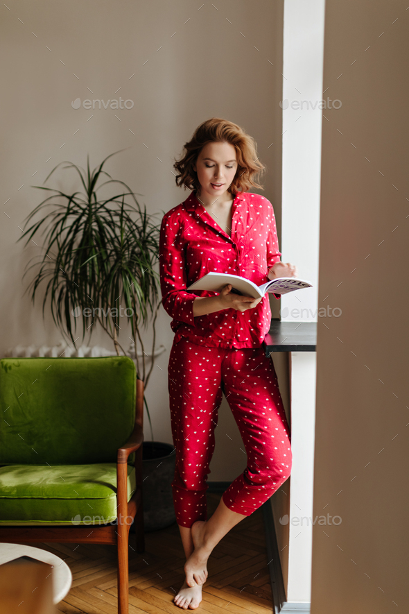 Full length view of barefoot lady reading magazing with interest ...