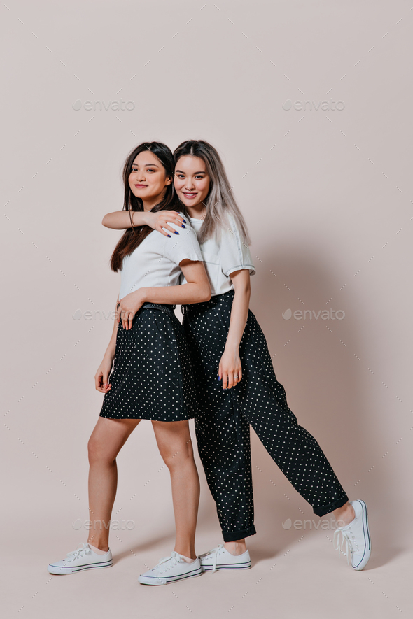 Full-length portrait of sisters in similar black outfit posing on beige ...