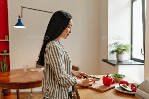 Charming woman posing in kitchen while cooking fresh vegetable salad ...