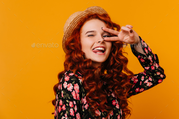 Mischievous girl with snow-white smile shows her tongue. Woman in straw ...