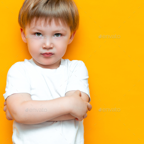 Portrait of angry little boy with arms folded isolated on yellow ...
