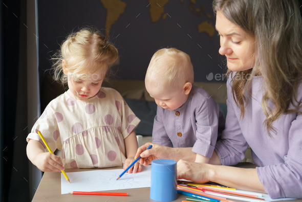 Caring young mom teaching how to draw her two little kids Stock Photo ...
