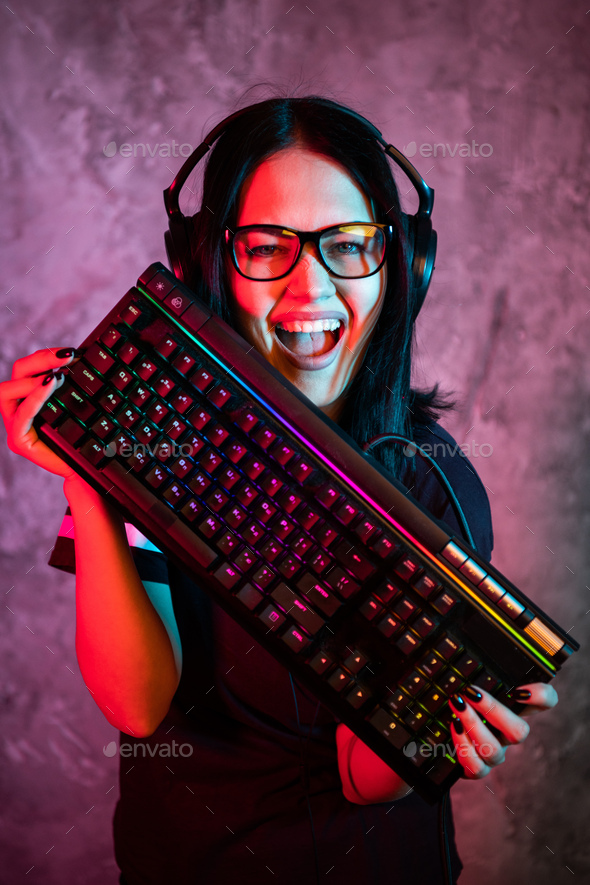 Nerd geek young adult women holding gaming keyboard over colorful pink ...