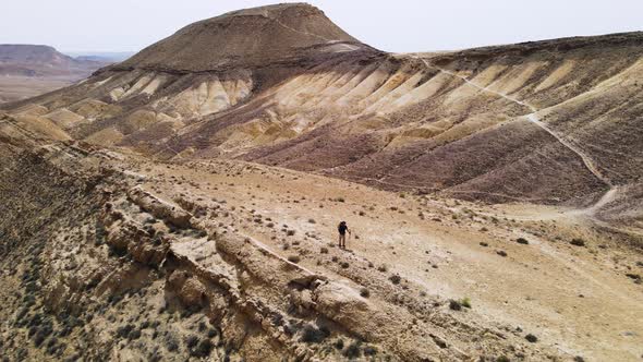 Aerial zoom out from hiker waving on Mount Ramon desert trail showing ...