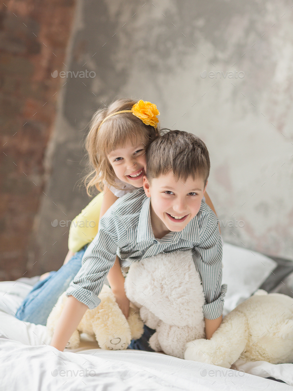 Brother and sister playing with teddy bear in bed Stock Photo by svittlana