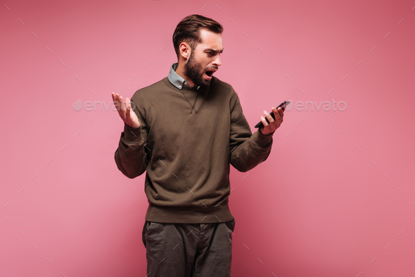 Man looks at phone screen in shock and posing on pink background. Stock ...