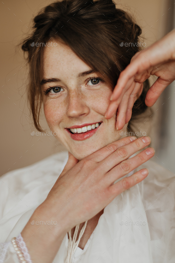 Charming young lady in white blouse smiles sincerely on beige ...
