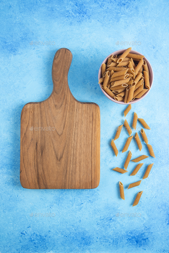 Vertical photo of raw brown penne pasta with wooden board Stock Photo ...