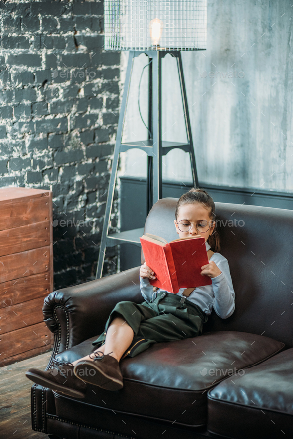 concentrated little child reading book on couch at home Stock Photo by ...