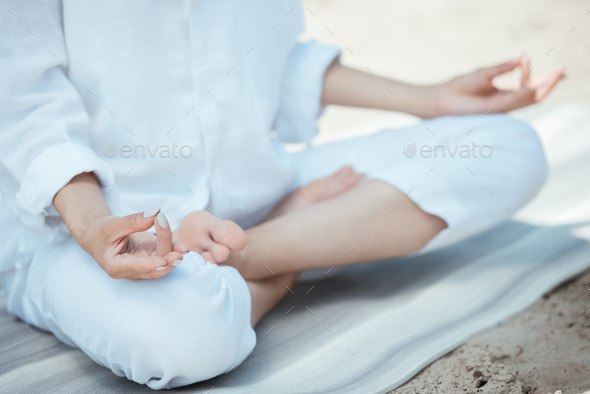 cropped image of woman in ardha padmasana (half lotus pose) on yoga mat ...