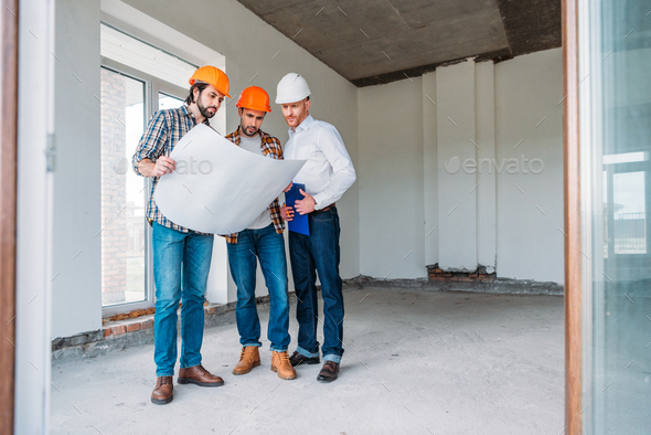 group of architects with blueprint having conversation inside of ...