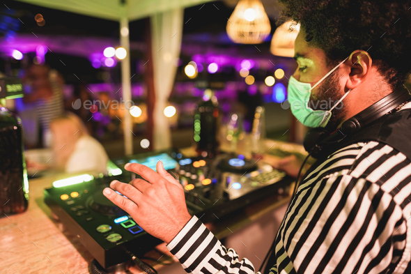 African dj playing music at cocktail bar while wearing face safety mask ...