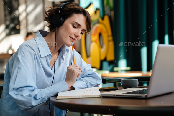 Focused girl writing down notes while using laptop and headphones Stock ...