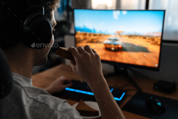 Caucasian guy eating sandwich while playing video game on his computer ... Caucasian guy eating sandwich while playing video game on his computer ...