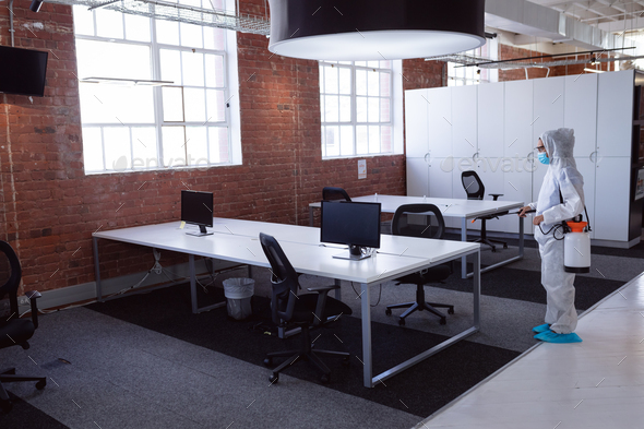 Cleaner wearing ppe suit, glasses and mask disinfecting office ...