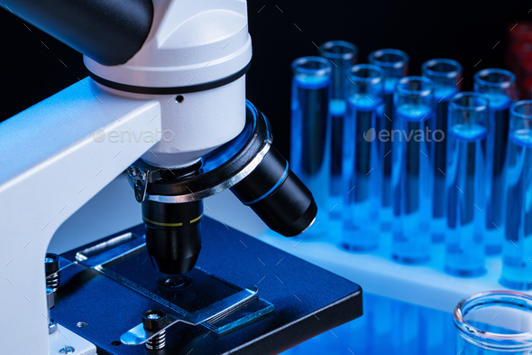 Close up of laboratory microscope with set of test tubes with blue ...