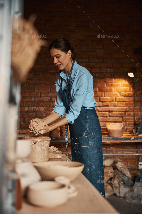 Happy cheerful brunette woman squeezing pieces of earthenware materials ...