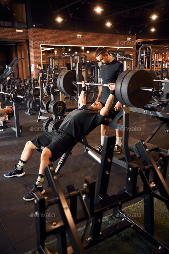 Hard-working man lifting weights with his friend back-up Stock Photo by ...