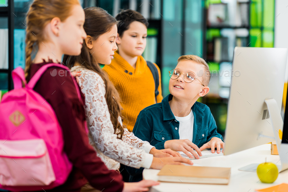 boy using desktop computer and looking at classmates in library Stock ...