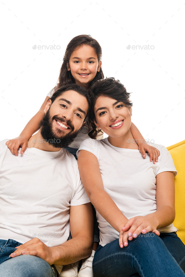 happy latin parents smiling while sitting on sofa near daughter ...