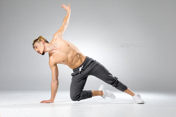 Young shirtless man performing dance movement while looking at distance ...