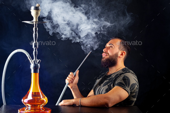 Bearded young man smoking shisha in a dark night club Stock Photo by ...
