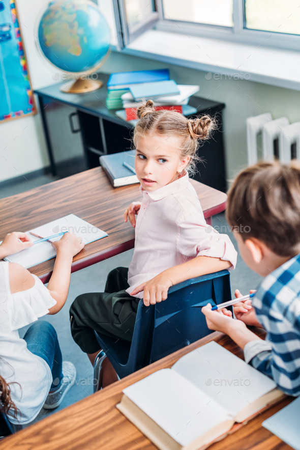 adorable schoolgirl looking back and talking to classmate Stock Photo ...