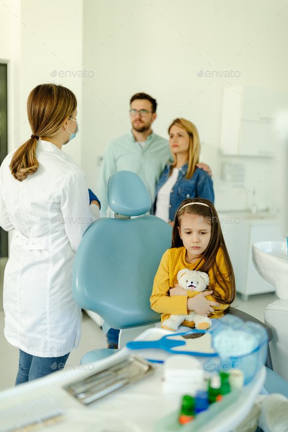 Child looks scared and hugging her toy while sitting in dental chair ...