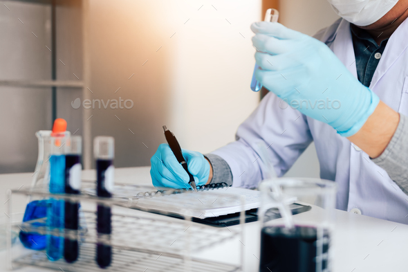 Scientist recording making note on book with his findings test tube in ...