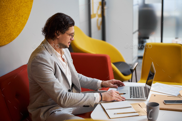 Serious brunette man sitting in front of laptop Stock Photo by Iakobchuk