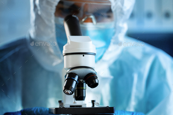 Medical worker in protective gown looking in microscope Stock Photo by ...
