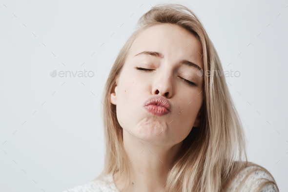 Attractive dreamy female model with blonde hair closes eyes, pouts lips ...