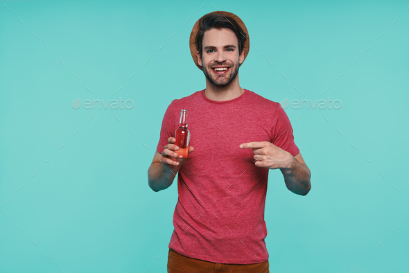 Handsome young smiling man holding bottle with drink and pointing it ...
