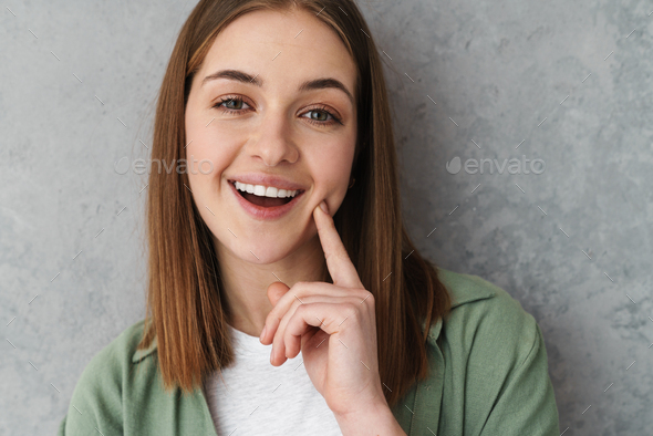 Happy beautiful nice girl smiling and pointing finger at her cheeks ...