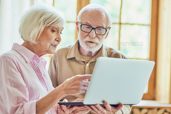 Elderly couple using computer near the window at their house Stock ...