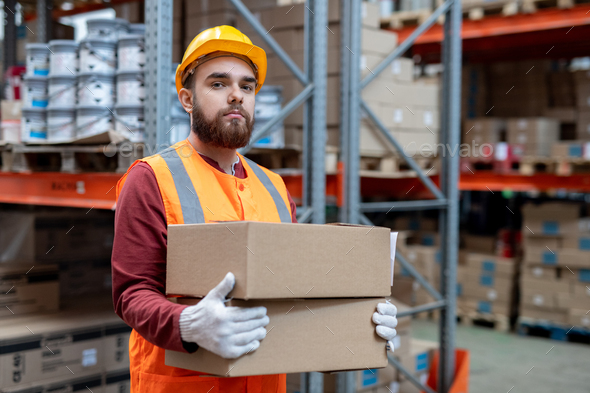 Gloved man in hardhat and workwear loading boxes Stock Photo by Pressmaster