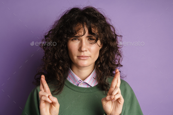 Brooding brunette curly girl thinking and holding hers fingers crossed ...